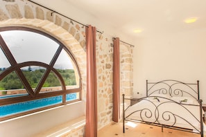 Quarto com parede de pedra, uma grande janela em arco e estrutura de cama em metal.