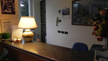Uma mesa de recepção com uma luminária, um quadro emoldurado, um telefone e um calendário na parede.