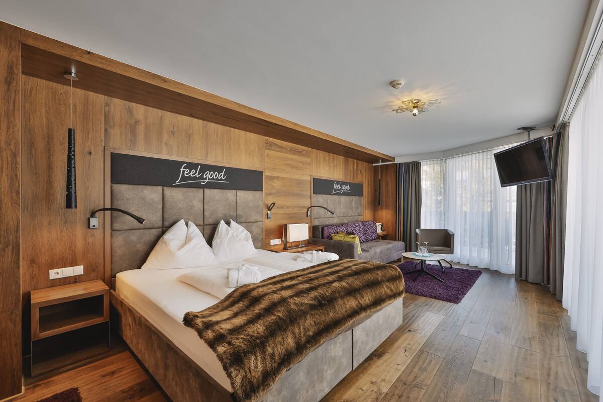 Quarto de hotel moderno com uma cama grande, televisão, escrivaninha e sofá.