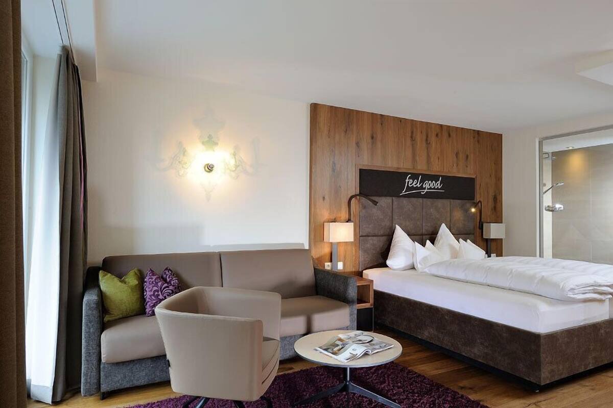 Quarto de hotel moderno com uma cama grande, um sofá, uma cadeira e uma pequena mesa.