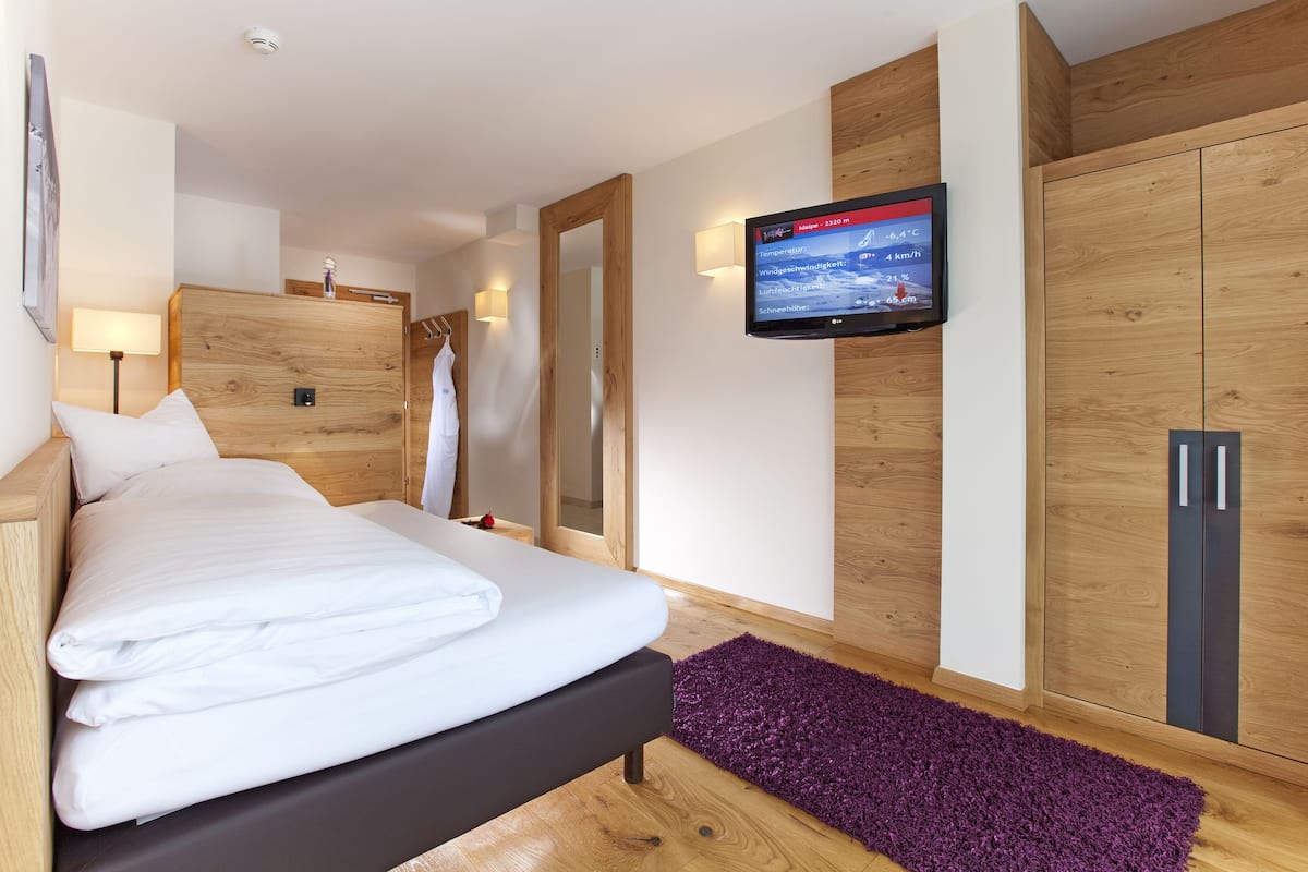 Quarto de hotel moderno com cama bem arrumada, guarda-roupa de madeira e uma televisão exibindo informações sobre o tempo.