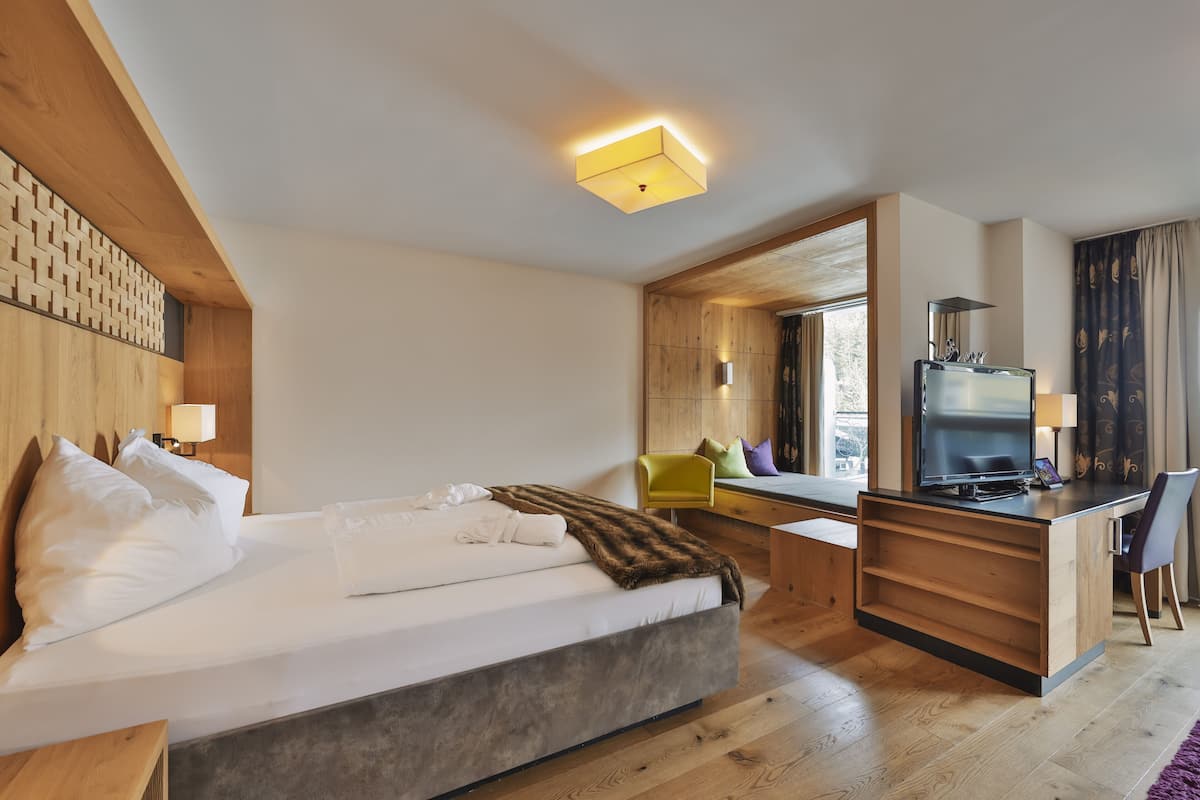 Quarto de hotel moderno com uma cama grande, uma escrivaninha, uma televisão e uma janela com cortinas.