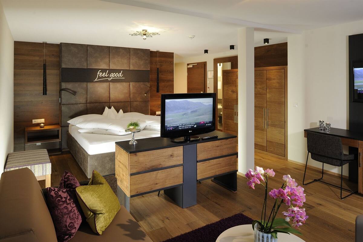 Quarto moderno com cama, televisão, cómoda de madeira e secretária.