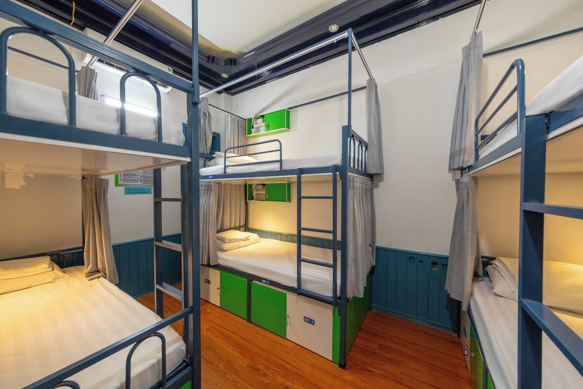 Quarto de dormitório com beliches, um pequeno armário verde e uma janela com cortinas.