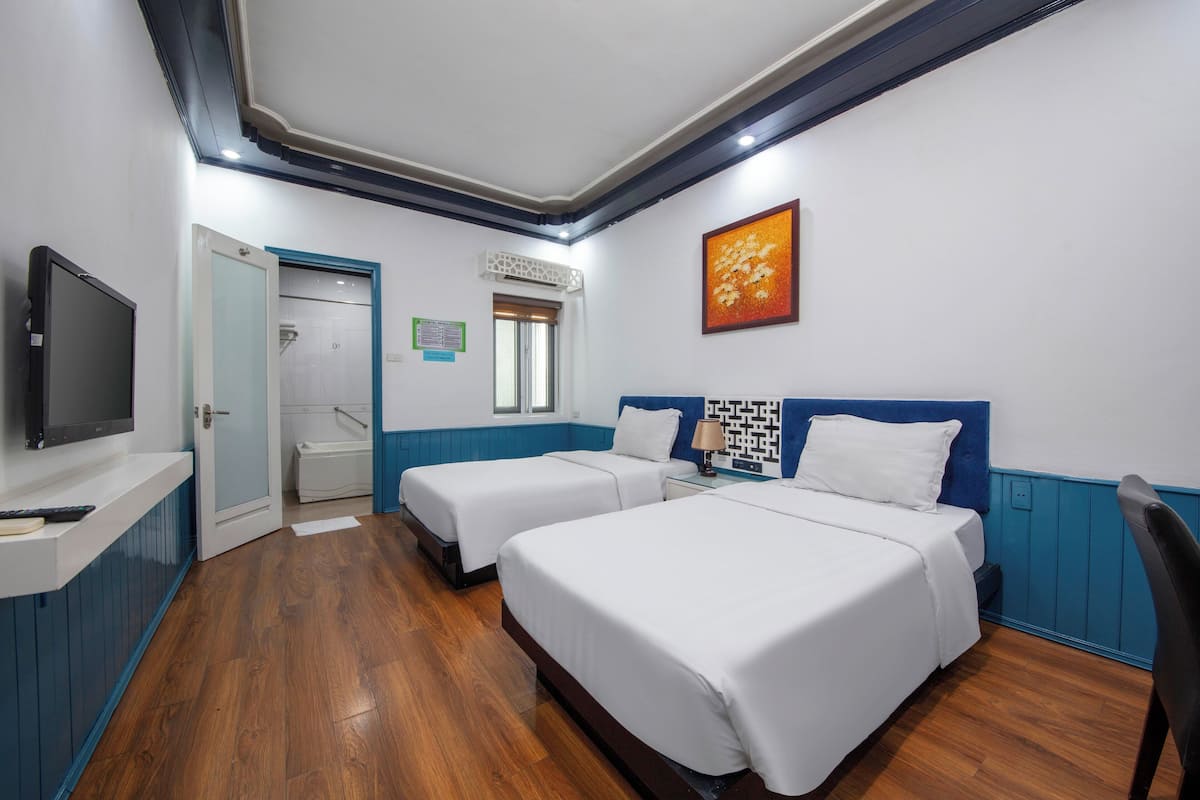 Quarto de hotel com duas camas, televisão, banheiro e um quadro na parede.