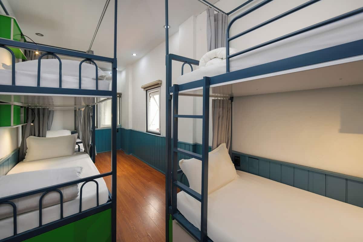 Quarto estilo dormitório com beliches, piso de madeira e janela com cortinas.