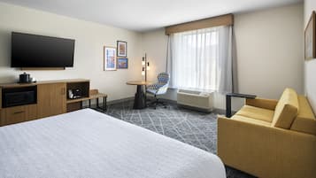 Quarto de hotel com uma cama grande, escrivaninha, cadeira, televisão e janela com cortinas.