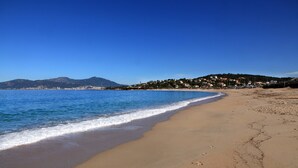Uma praia com águas azul-claras, uma orla arenosa e uma cordilheira ao longe.