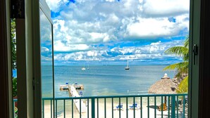 Uma varanda com vista para o mar, uma praia e uma cabana de palha.