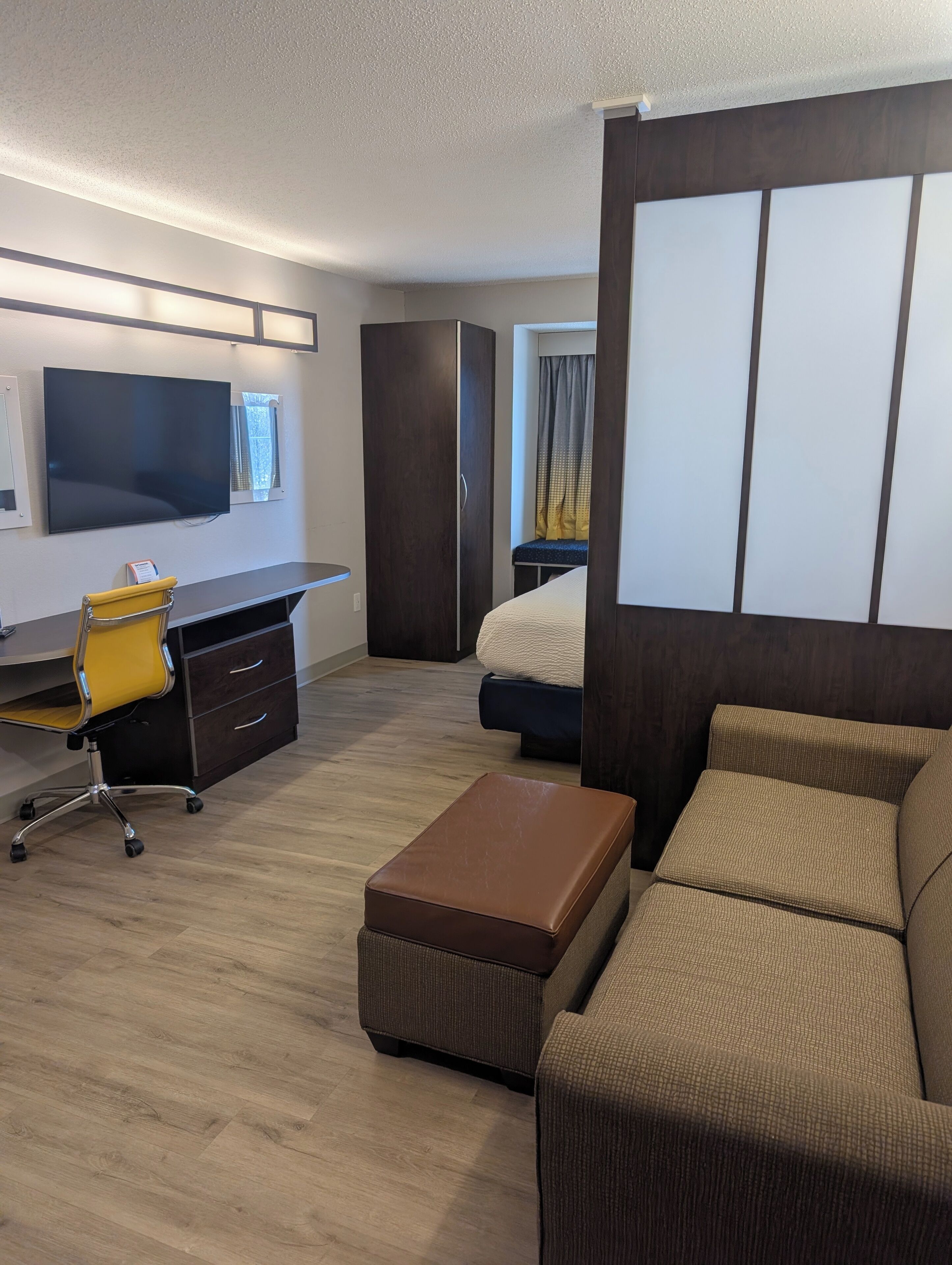 Quarto de hotel com cama, sofá, escrivaninha com cadeira, televisão e guarda-roupa.