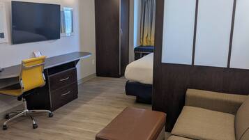 Quarto de hotel com cama, sofá, escrivaninha com cadeira, televisão e guarda-roupa.
