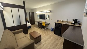 Quarto de hotel compacto com sofá, pequena escrivaninha, cozinha compacta e espelho.