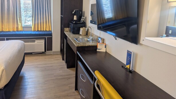 Quarto de hotel compacto com cama, cozinha compacta, televisão de tela plana e um espelho grande.