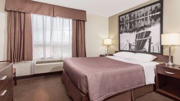 Quarto de hotel com uma cama grande, duas luminárias de cabeceira, uma cadeira, uma escrivaninha e uma janela com cortinas.