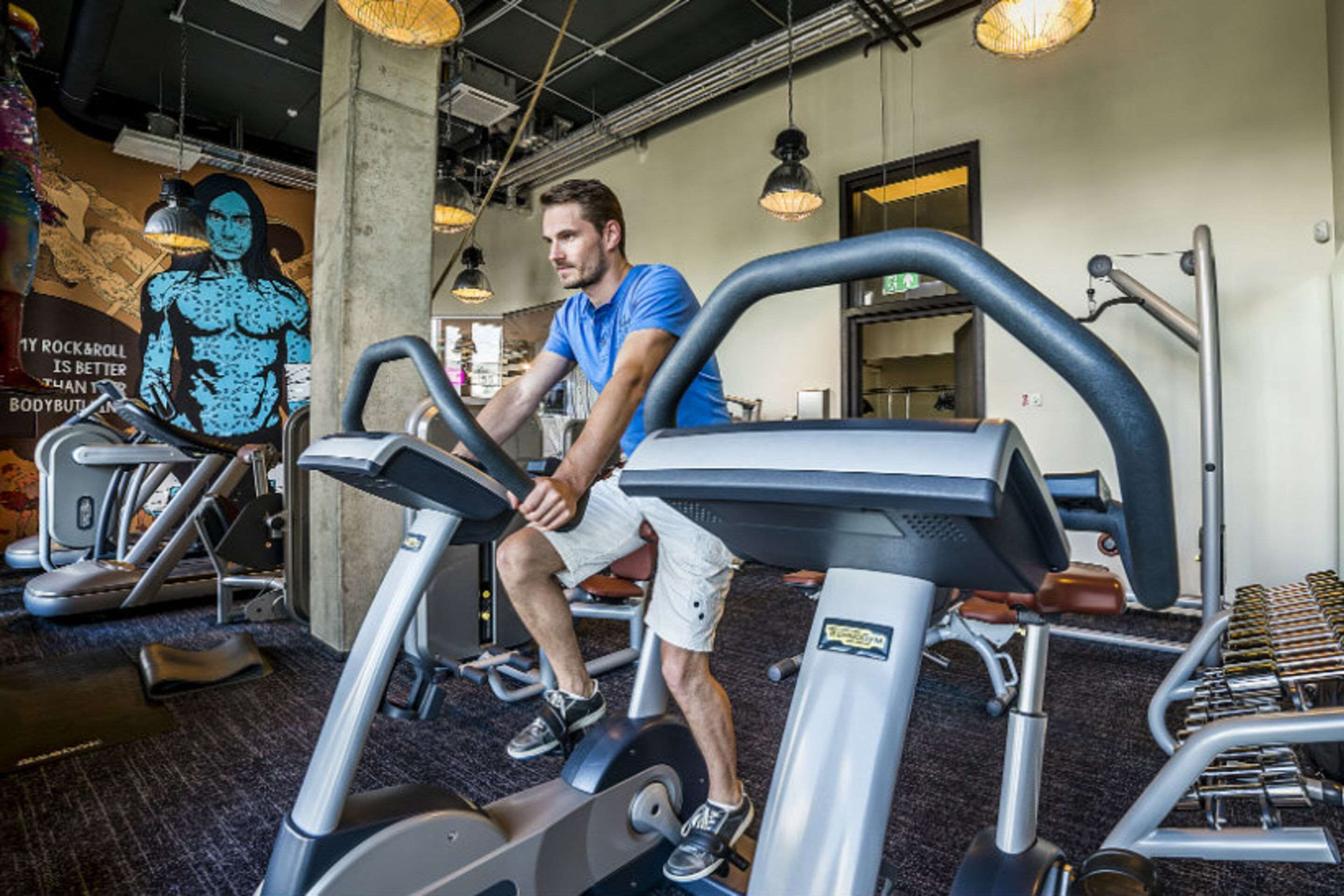 Uma academia com esteiras, um mural na parede e equipamentos de exercícios.