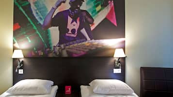 Quarto de hotel com duas camas de solteiro, cabeceira escura e uma tela grande exibindo um DJ.