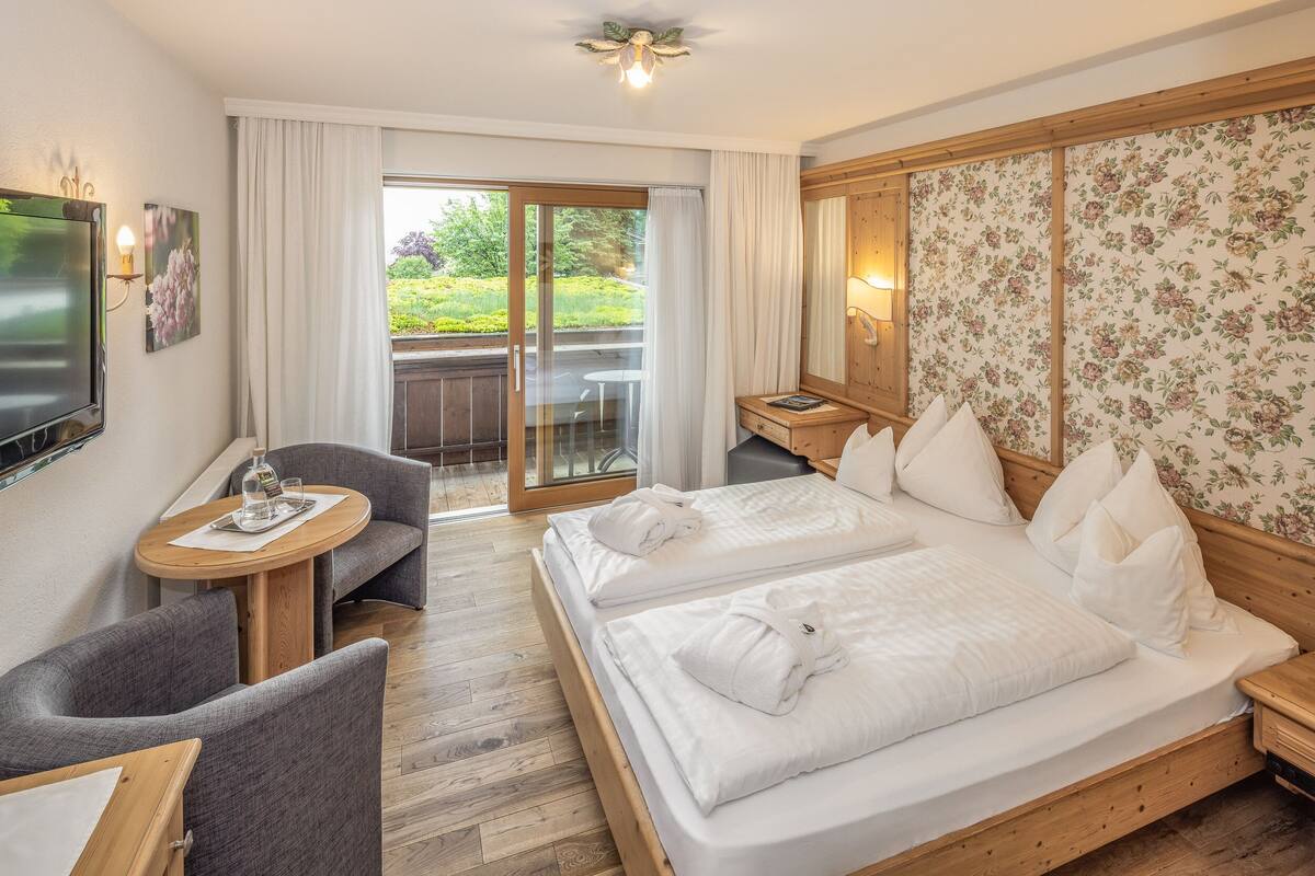 Quarto de hotel com cama, escrivaninha, cadeira e televisão.