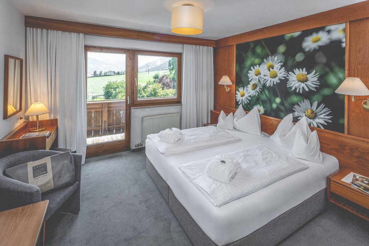 Quarto de hotel com uma cama grande, uma cadeira, uma escrivaninha e vista para o exterior.