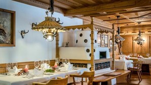 Uma sala de jantar com mesas e cadeiras de madeira, lareira e luminárias fixadas na parede.