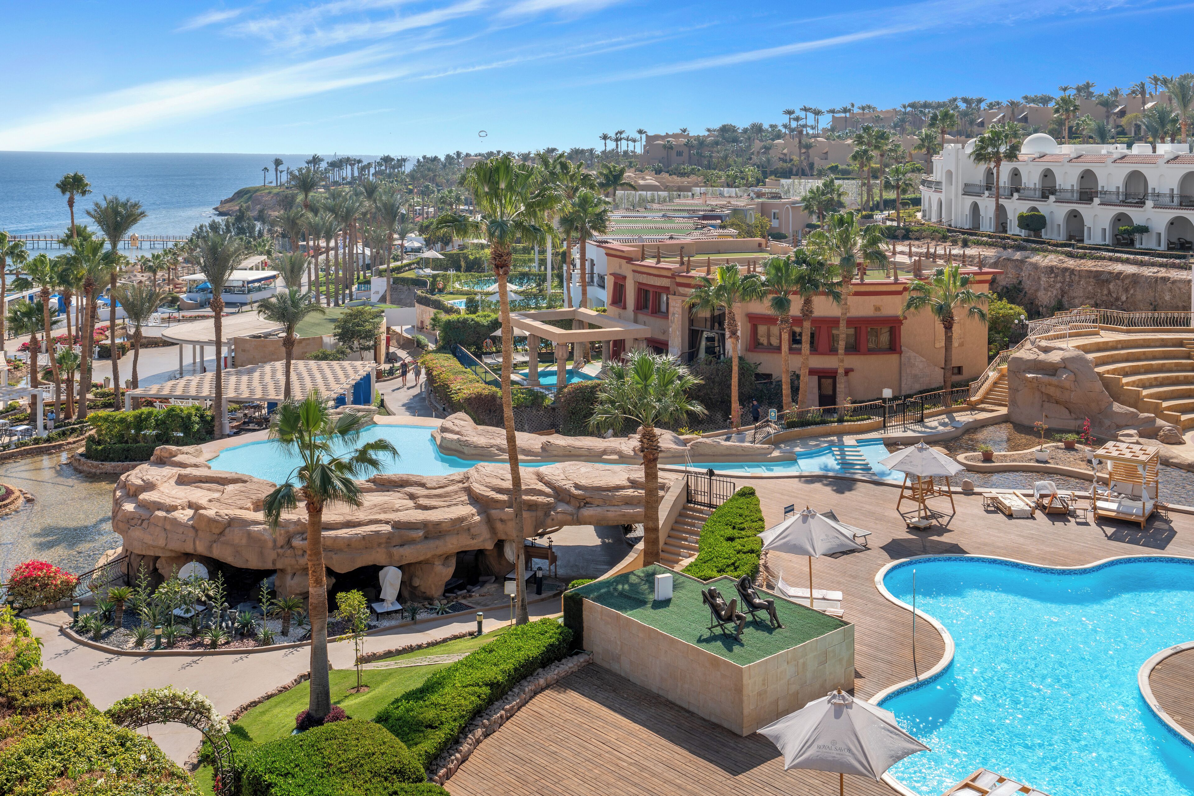 Um resort com várias piscinas, palmeiras e vista para o oceano.