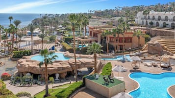 Um resort com várias piscinas, palmeiras e vista para o oceano.