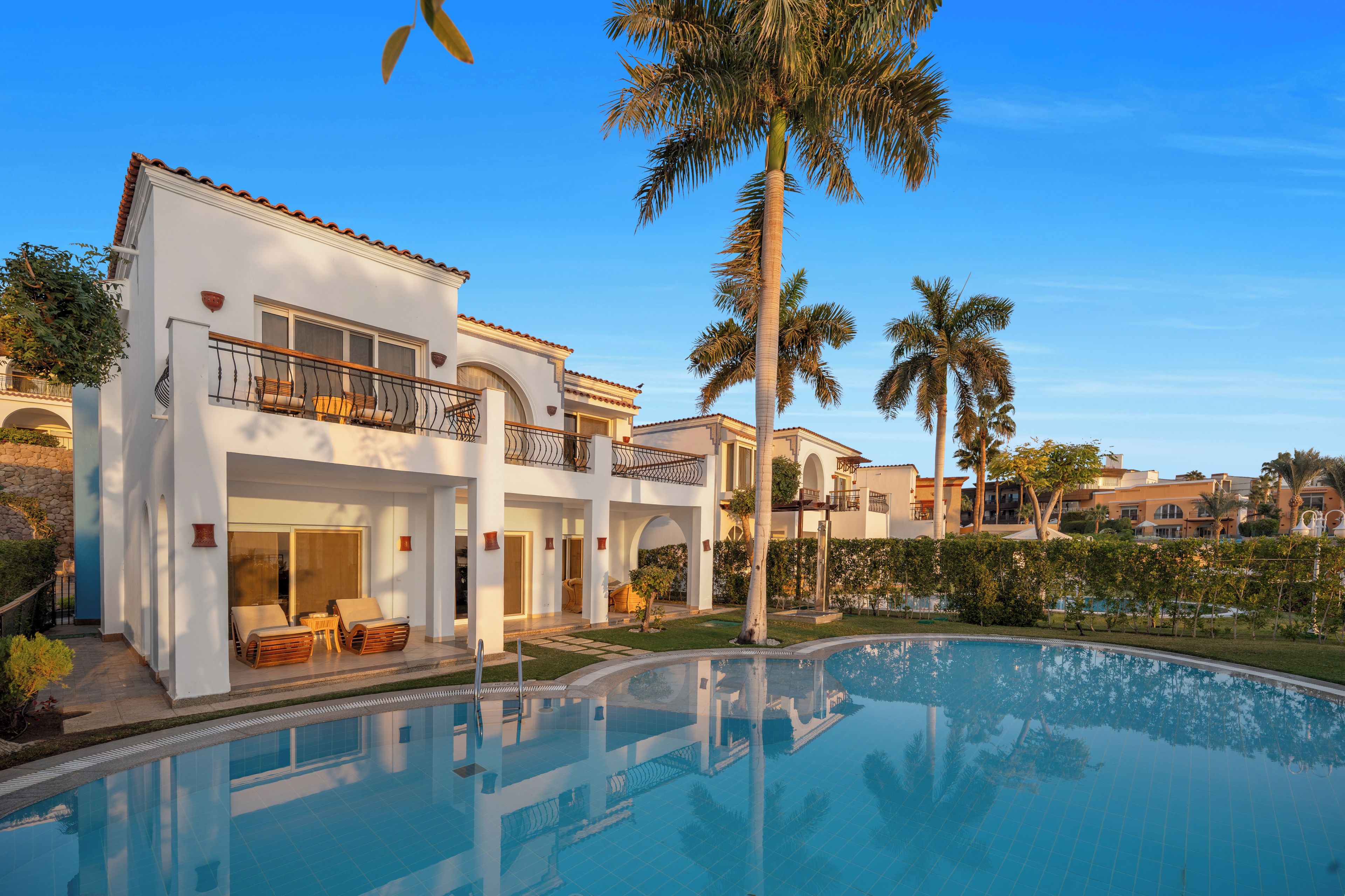 Uma casa de dois andares com piscina, área de estar externa e palmeiras.