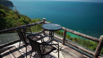 Um deck de madeira com uma mesa de vidro e duas cadeiras com vista para a costa.
