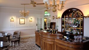 Uma área de bar com balcão de madeira, vários bancos altos e uma adega bem abastecida.