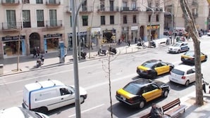 Vista da rua com uma fileira de edifícios altos, uma van branca e vários carros, incluindo um táxi amarelo.