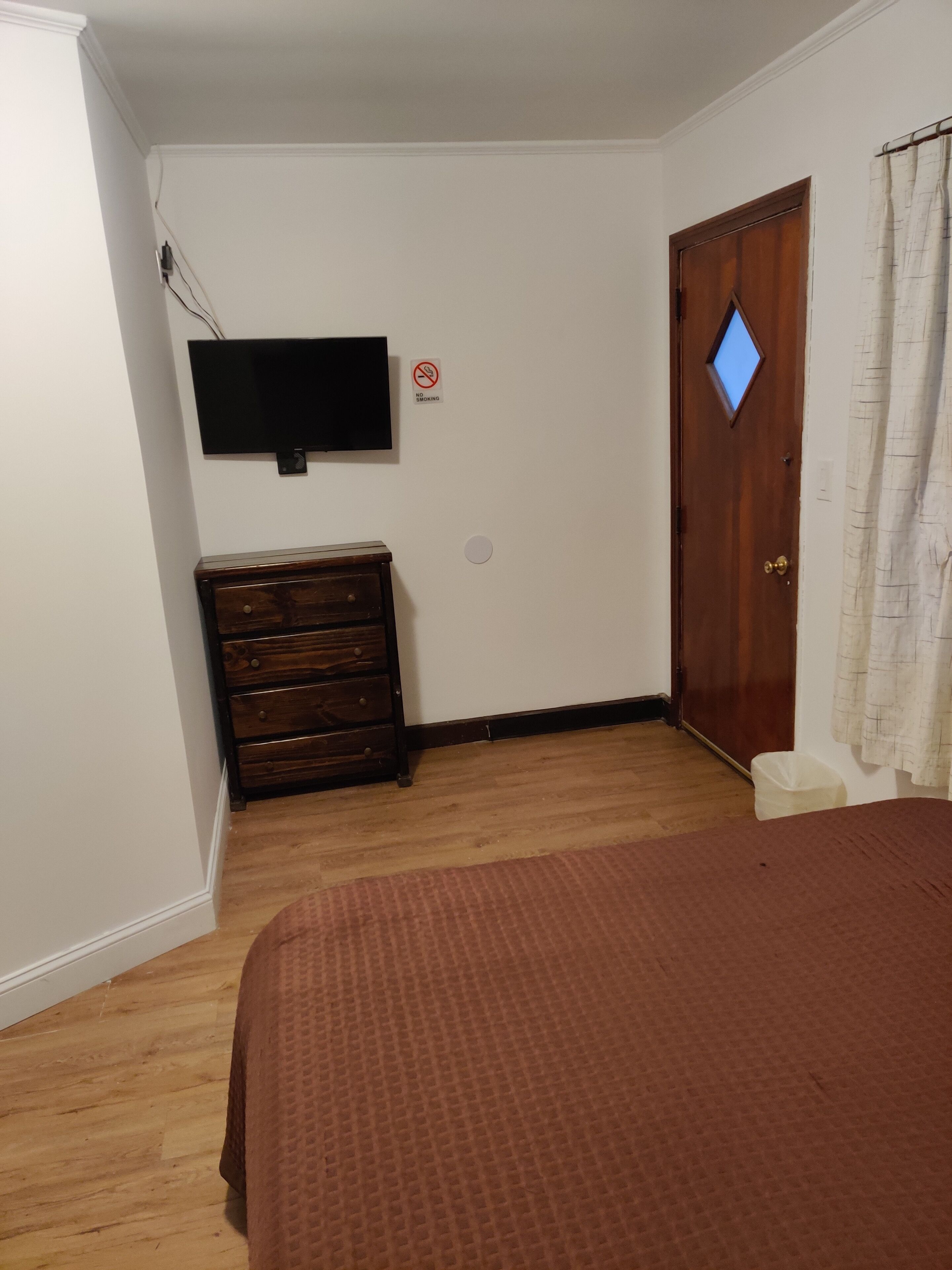 Quarto com cama, penteadeira, televisão e porta com olho mágico.