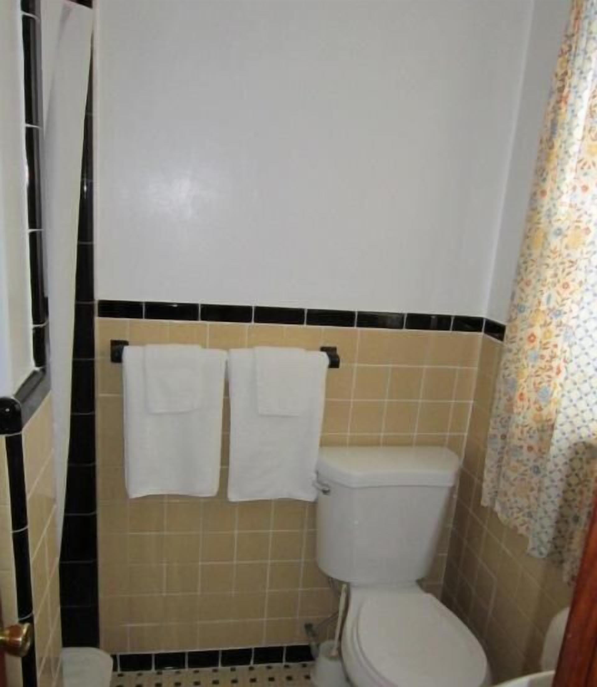Casa de banho com sanita, duas toalhas brancas penduradas numa barra e cortina de chuveiro estampada com motivos florais.