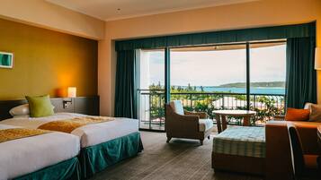 Quarto de hotel com duas camas, uma varanda com vista para o mar e uma área de estar com uma mesa.