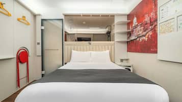 Quarto de hotel com cama, uma cadeira vermelha, televisão presa à parede e uma pintura com vista para a cidade.
