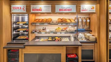 Buffet de café da manhã com seções identificadas para veganos, sem glúten e itens de café da manhã, incluindo pães e frutas.