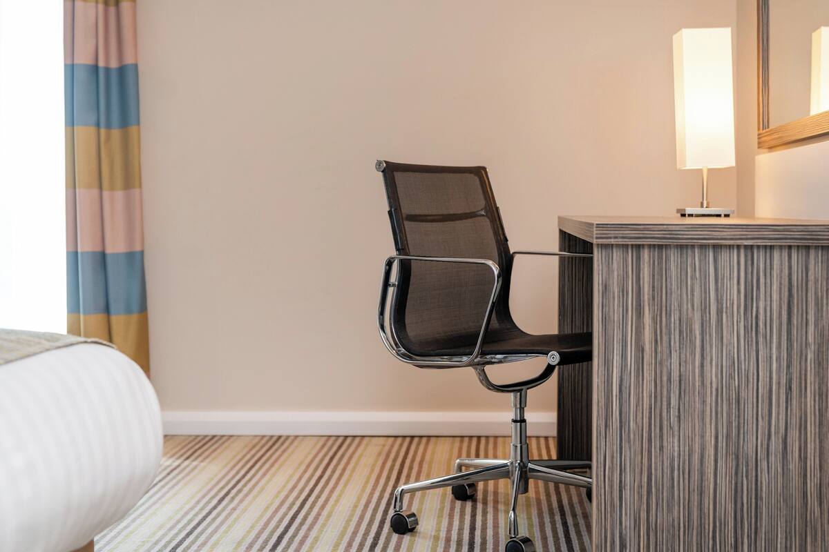 Quarto de hotel com uma cama, uma escrivaninha com candeeiro e uma cadeira.