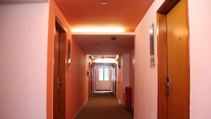 Corredor com portas de madeira, um alarme de incêndio e uma placa indicando a saída.