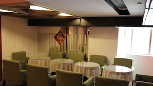 Quarto com cadeiras verdes e mesas redondas, um ornamento decorativo pendurado e uma janela com persianas.
