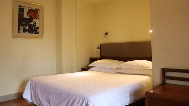 Quarto de hotel com uma cama de solteiro, cabeceira de madeira, mesa de cabeceira e um quadro abstrato emoldurado na parede.