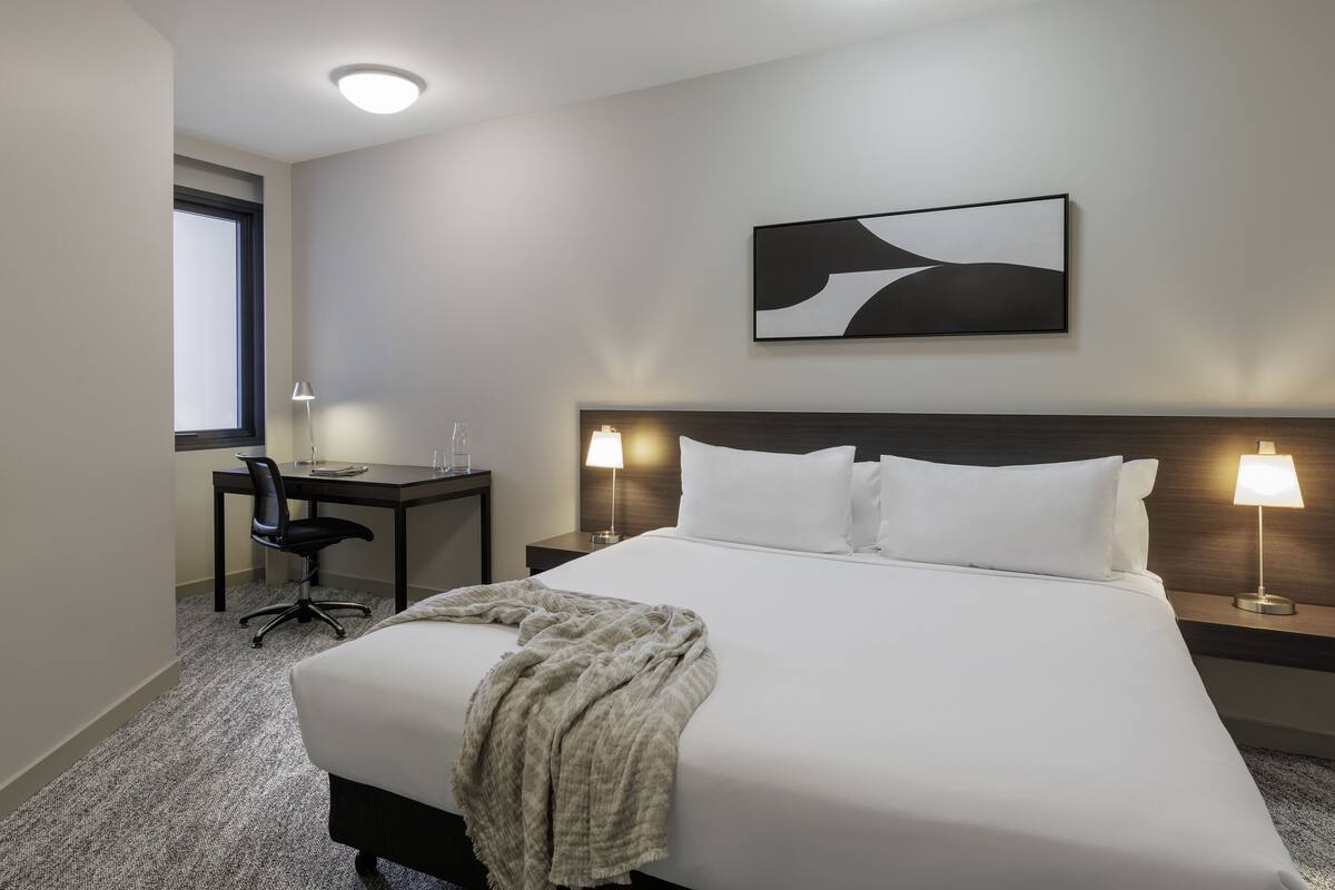 Quarto de hotel com uma cama grande, uma escrivaninha e duas luminárias de cabeceira.
