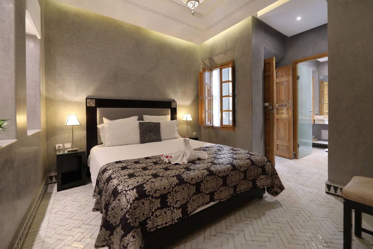 Quarto de hotel com uma cama grande, duas mesas de cabeceira e uma porta de madeira.