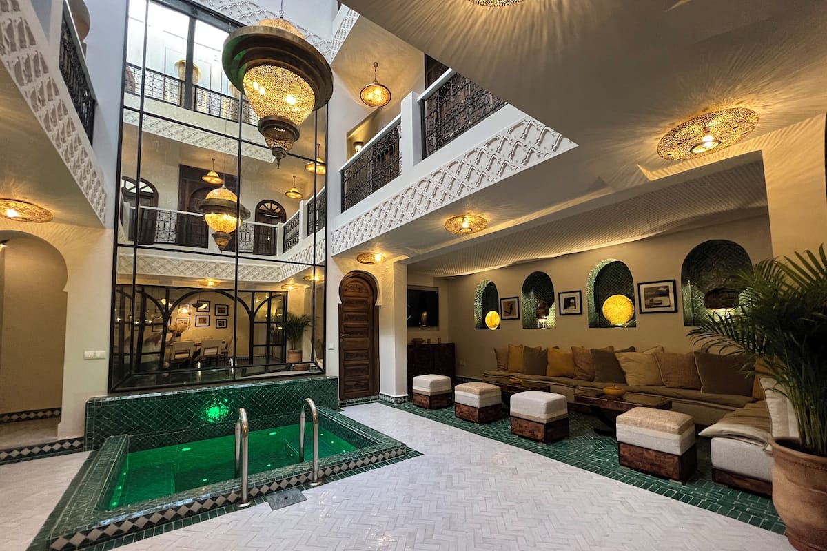 Amplo espaço interno com piscina central, vários espaços para sentar e teto alto com iluminação decorativa.