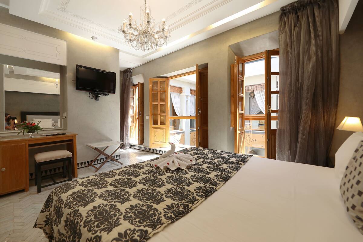 Quarto de hotel com cama, escrivaninha, cadeira, televisão e lustre.