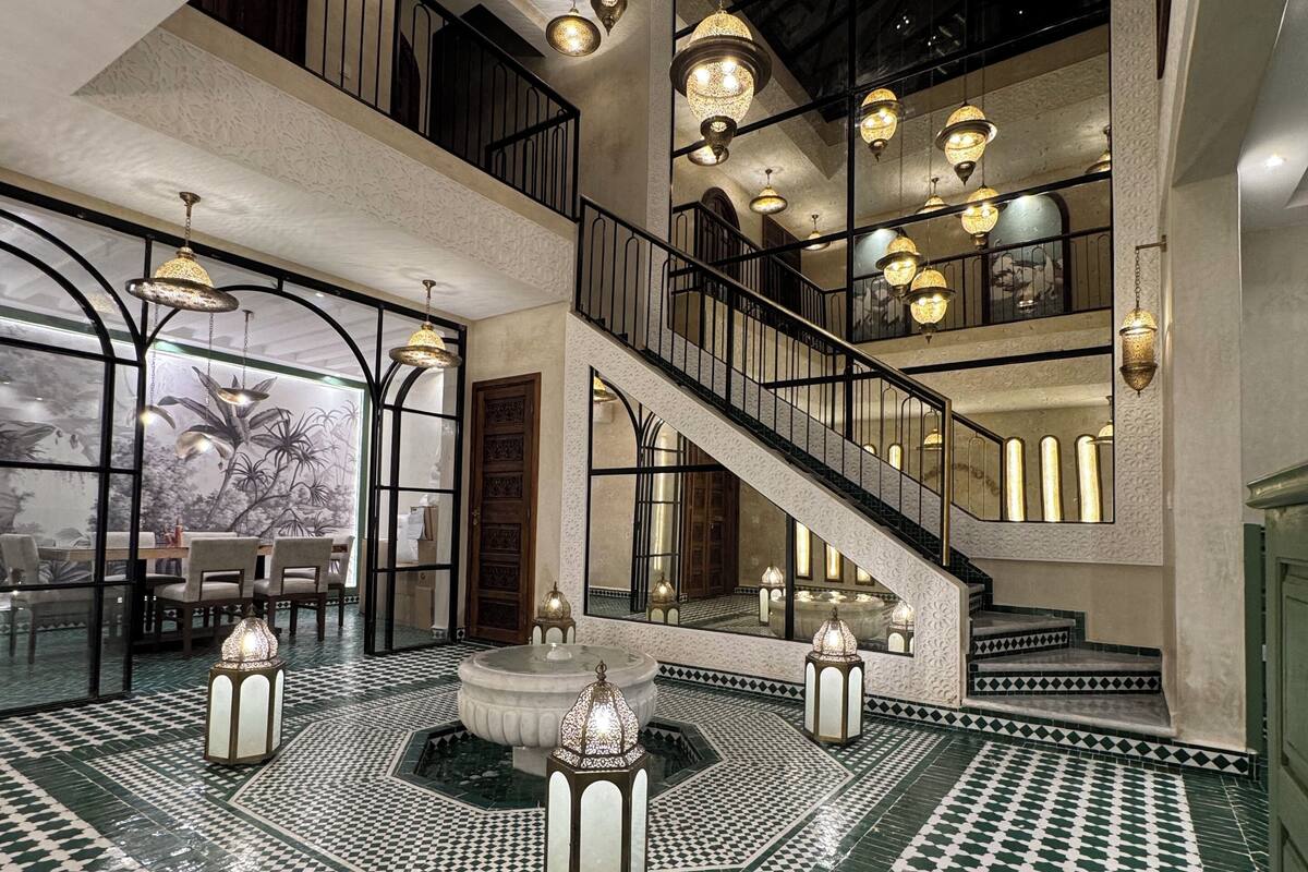 Um hall amplo com uma fonte, piso xadrez e várias escadarias.