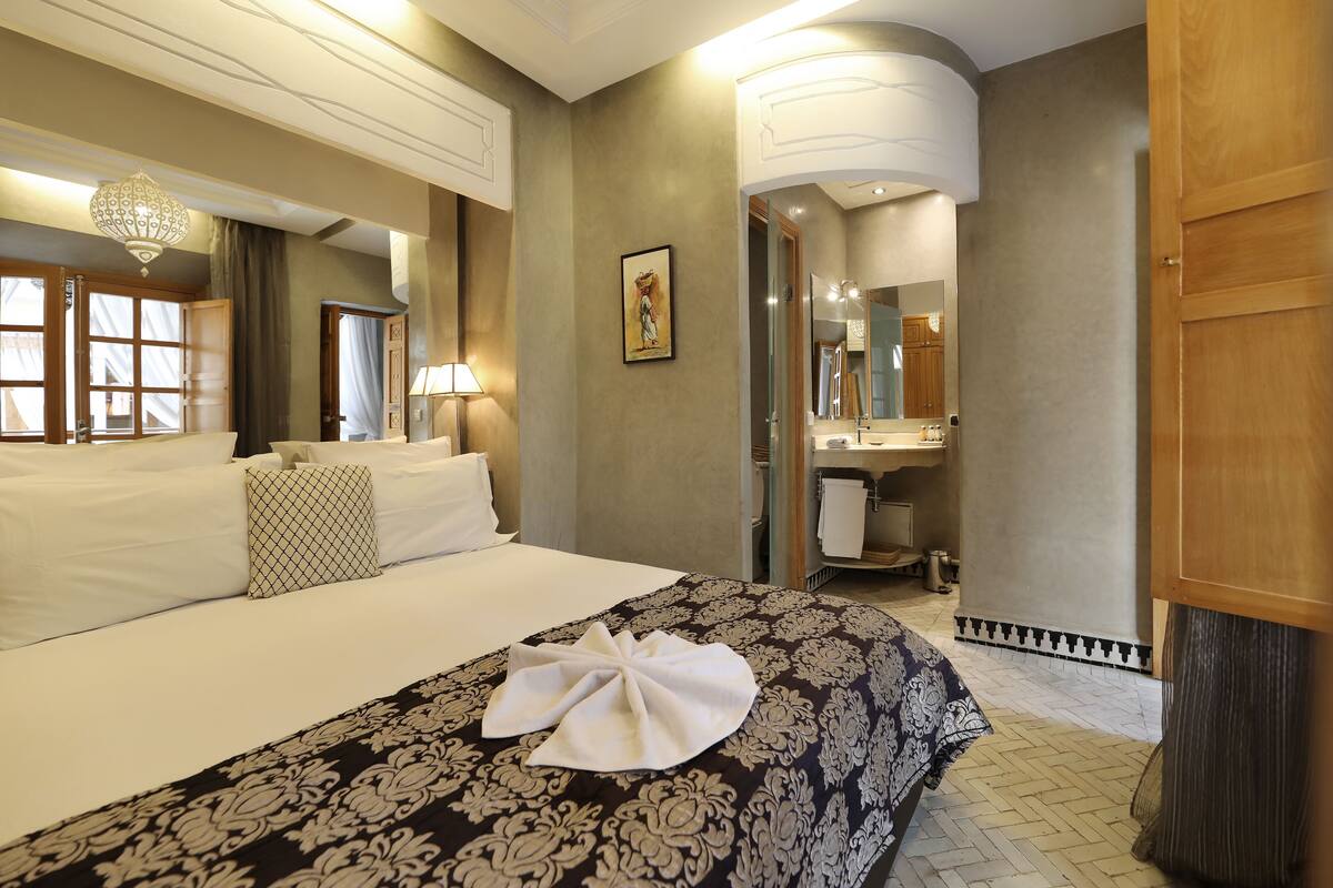 Quarto de hotel com uma cama grande, banheiro com espelho e lustre.