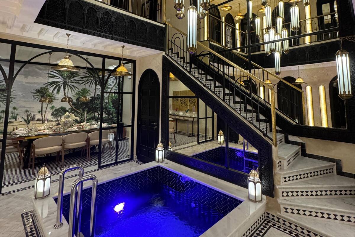 Uma área de piscina interior luxuosa, com piscina central, vários níveis com varandas e luminárias ornamentadas.