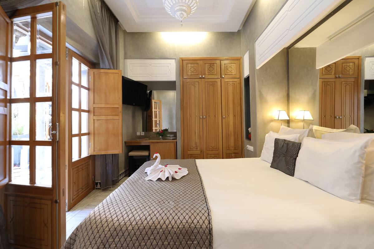 Quarto de hotel com cama, guarda-roupa de madeira, escrivaninha e espelho.