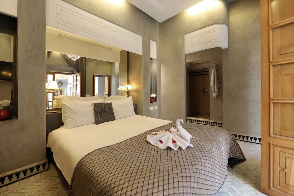 Quarto de hotel com uma cama grande, um espelho, chuveiro e guarda-roupa de madeira.