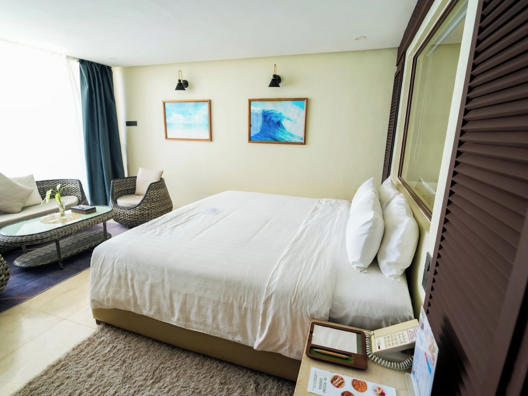 Quarto de hotel com cama, uma cadeira, uma mesinha e duas luminárias fixadas na parede.