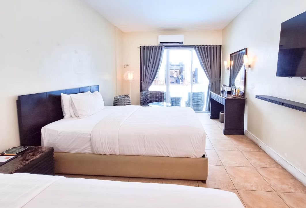 Quarto de hotel com uma cama grande, uma escrivaninha com cadeira, televisão e vista para o exterior.