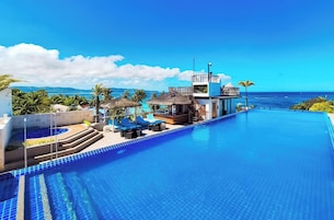 Piscina do resort com vista para o oceano, área de estar com guarda-sóis e um edifício com varanda com vista para a água.